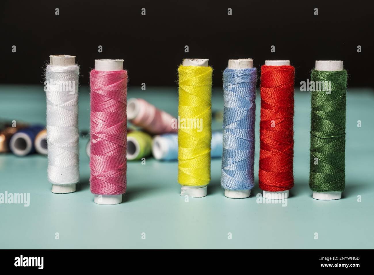 New spools of multi colored thread standing on a smooth light blue ...