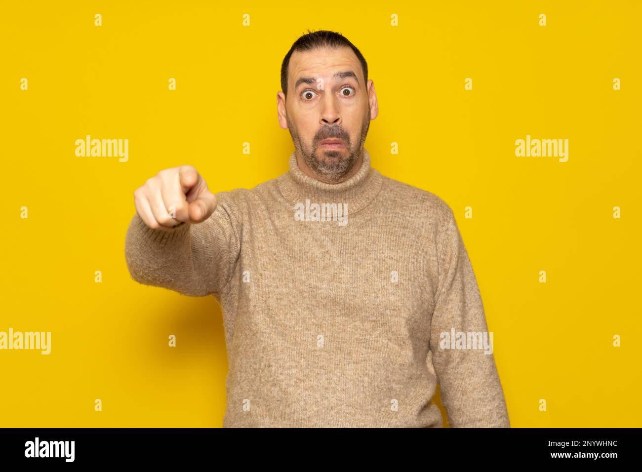 Bearded hispanic man in his 40s wearing a beige turtleneck pointing at ...