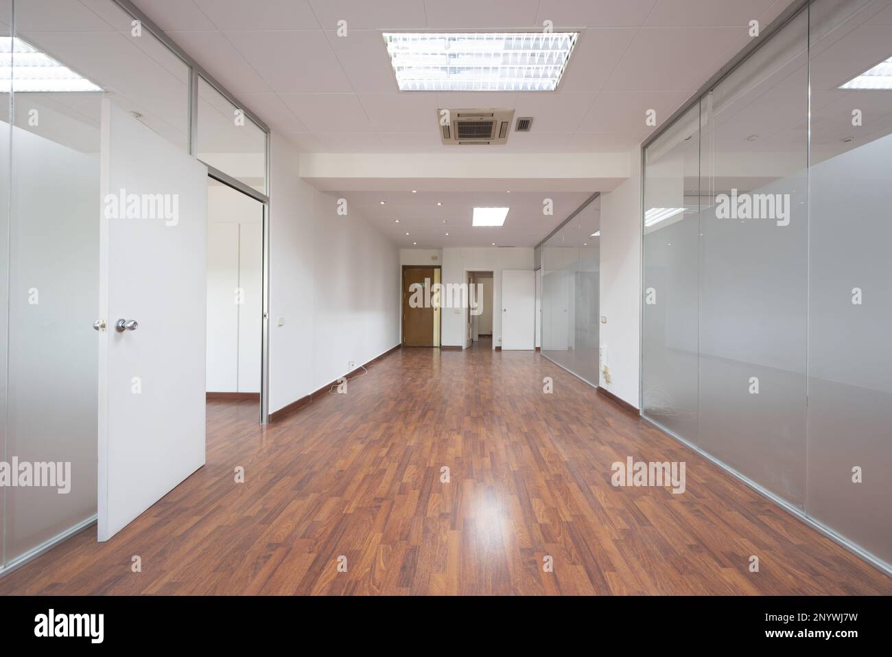 Empty offices with technical ceilings, white walls, reddish wooden ...