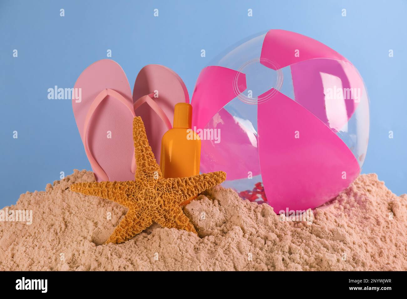 Beach ball, sunscreen, flip flops and starfish on sand against light ...