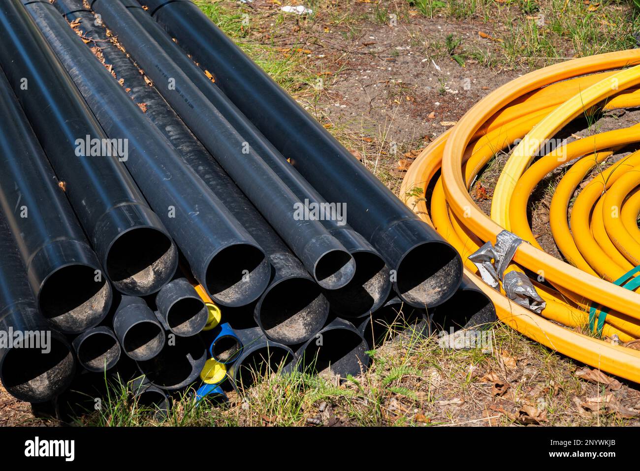 Plastic black pipes lying on the ground next to a roll of yellow cable ...