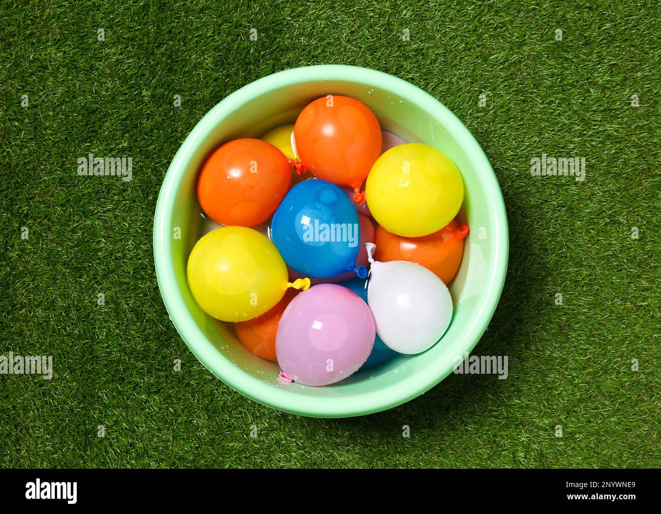 Basin full of colorful water bombs on green grass, top view Stock Photo ...