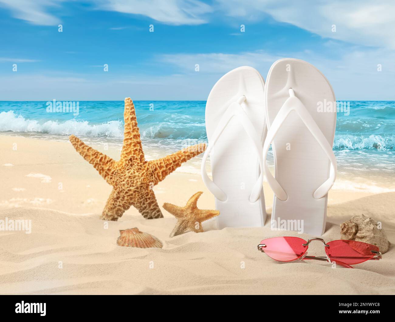 White flip flops, starfishes, sea shells and sunglasses on sandy beach ...