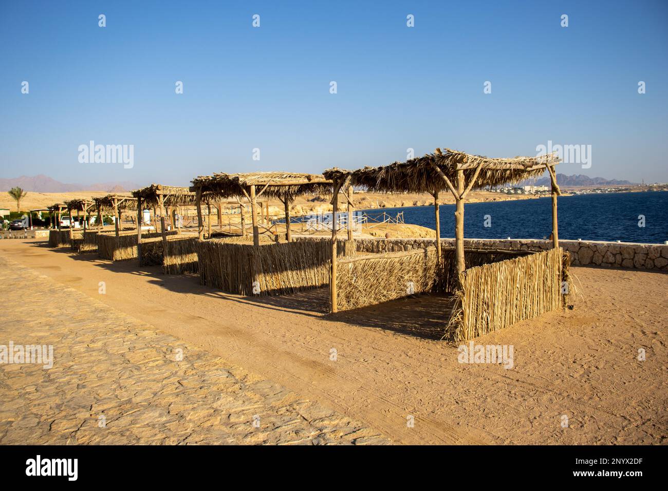 empty beach huts made of straw next to dark blue sea Stock Photo - Alamy