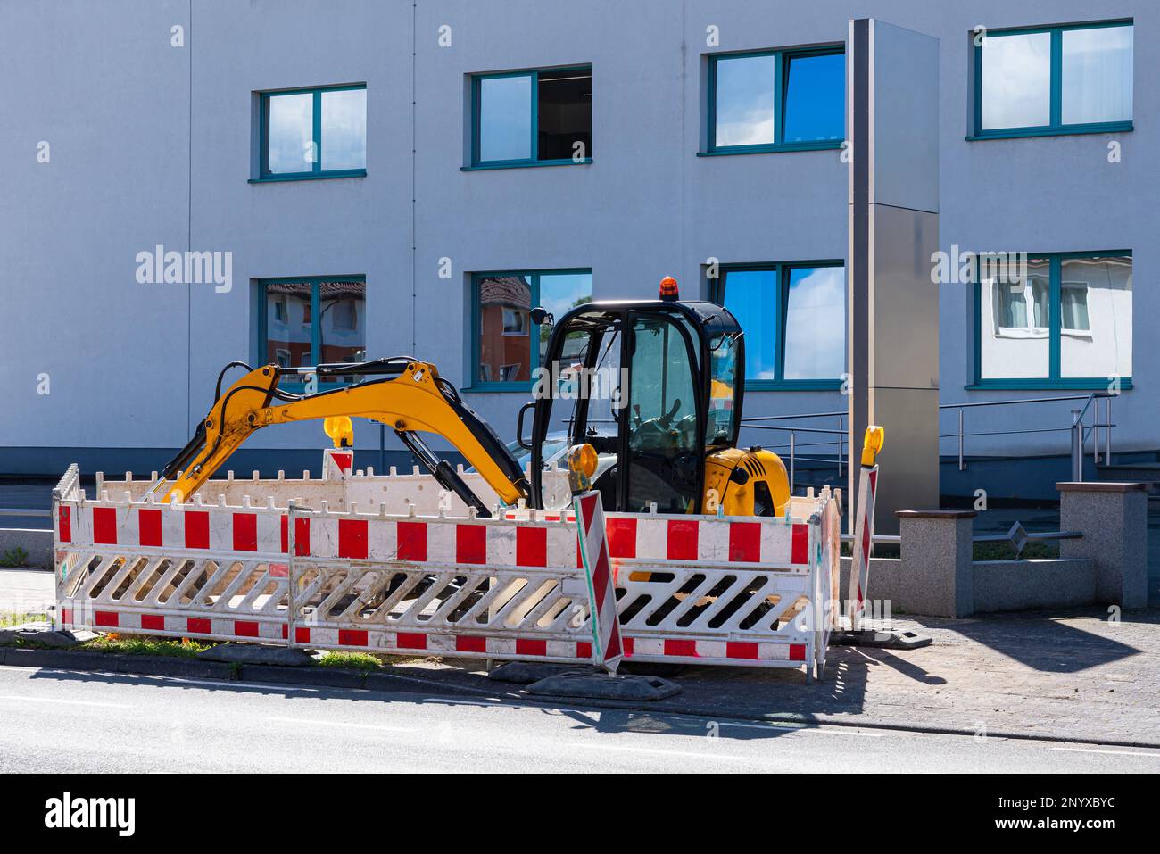 Yellow excavator fenced with traffic barriers. Light building with ...