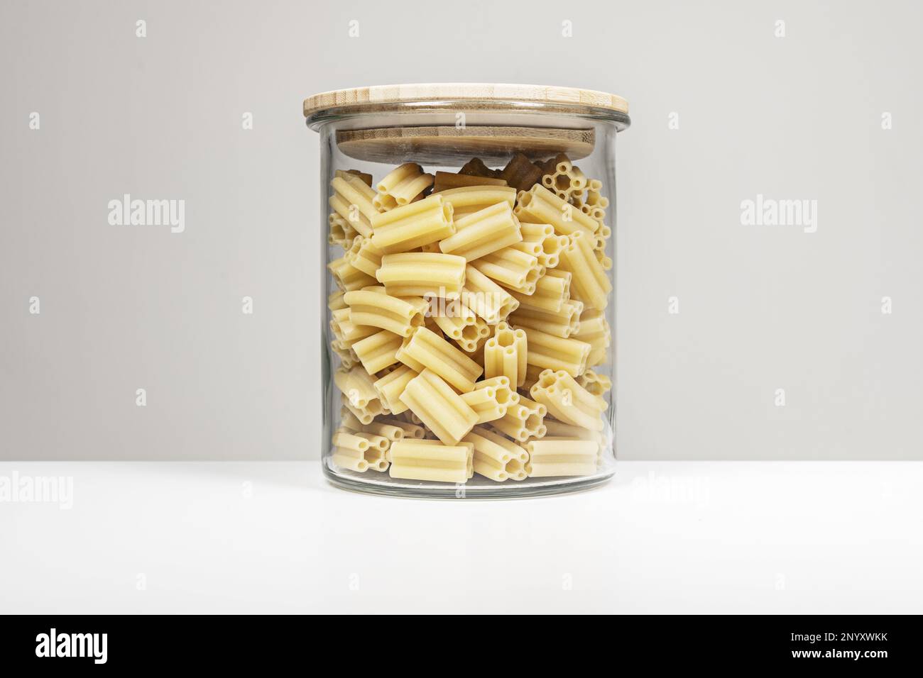 Glass jar with a wooden lid filled with dried pasta for cooking on a ...