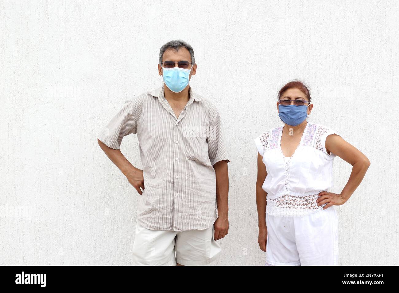 Older Latino couple with protective face masks on white wall background ...