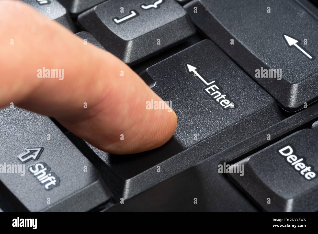 Finger pressing the enter key on a simple black computer keyboard ...
