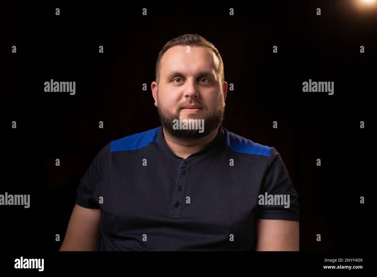 Portrait of a large young man with a beard. Dark background. Looks into ...