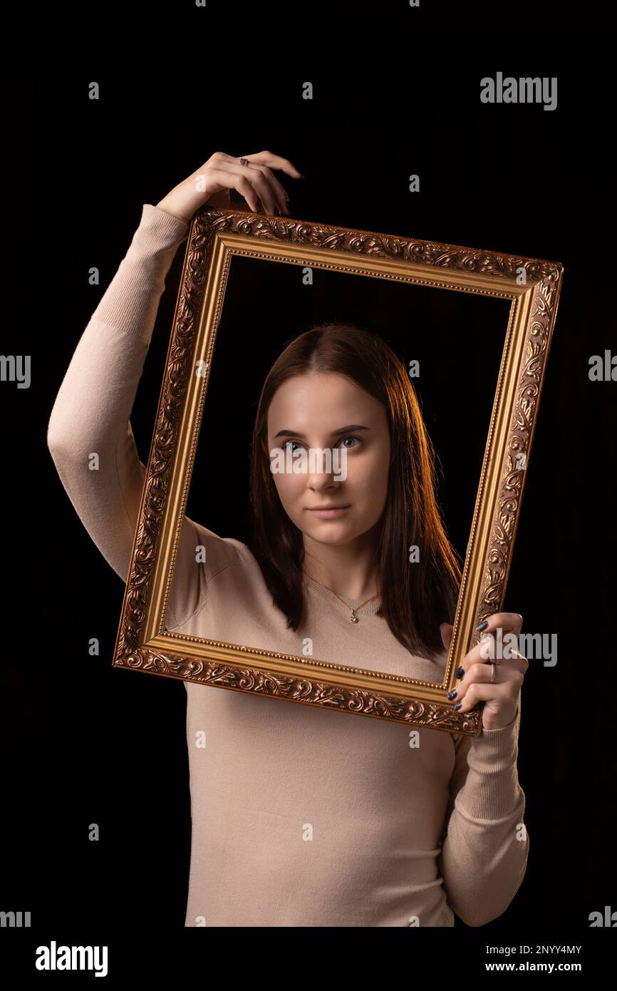 A young woman is holding a picture frame. Black background ...