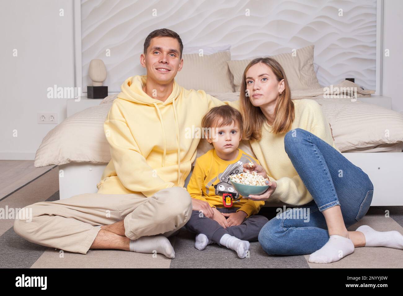 Friendly family, parents with child son sitting by the bed and holding ...