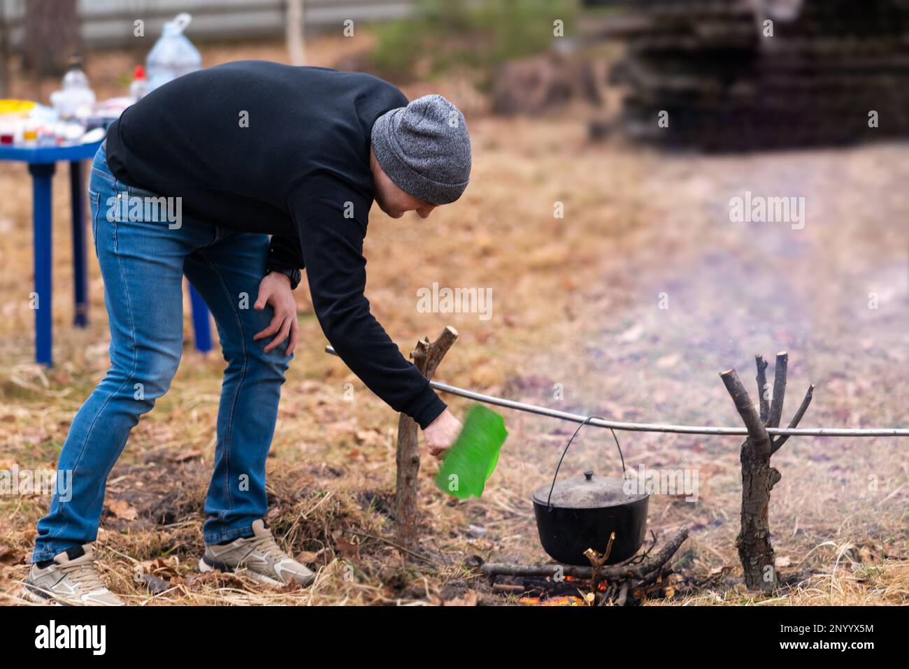 A young man is fanning a fire with a plastic spatula to cook food in a ...