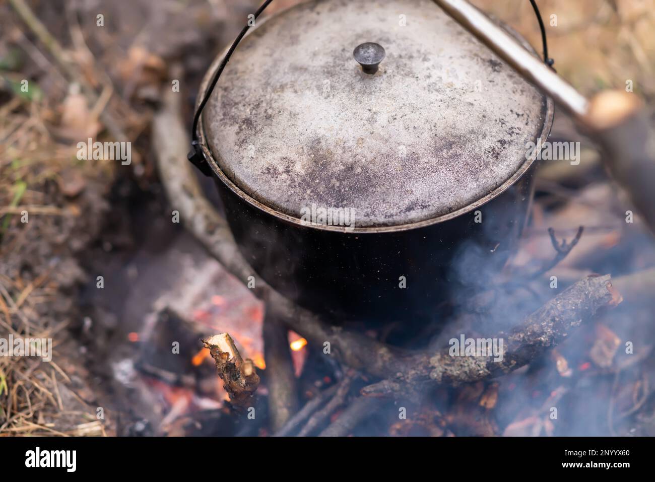 Top view of a cast iron pot with a lid hanging over a burning campfire ...