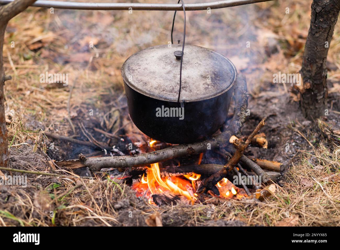 Close-up of a cast-iron cauldron with a lid suspended over a burning ...