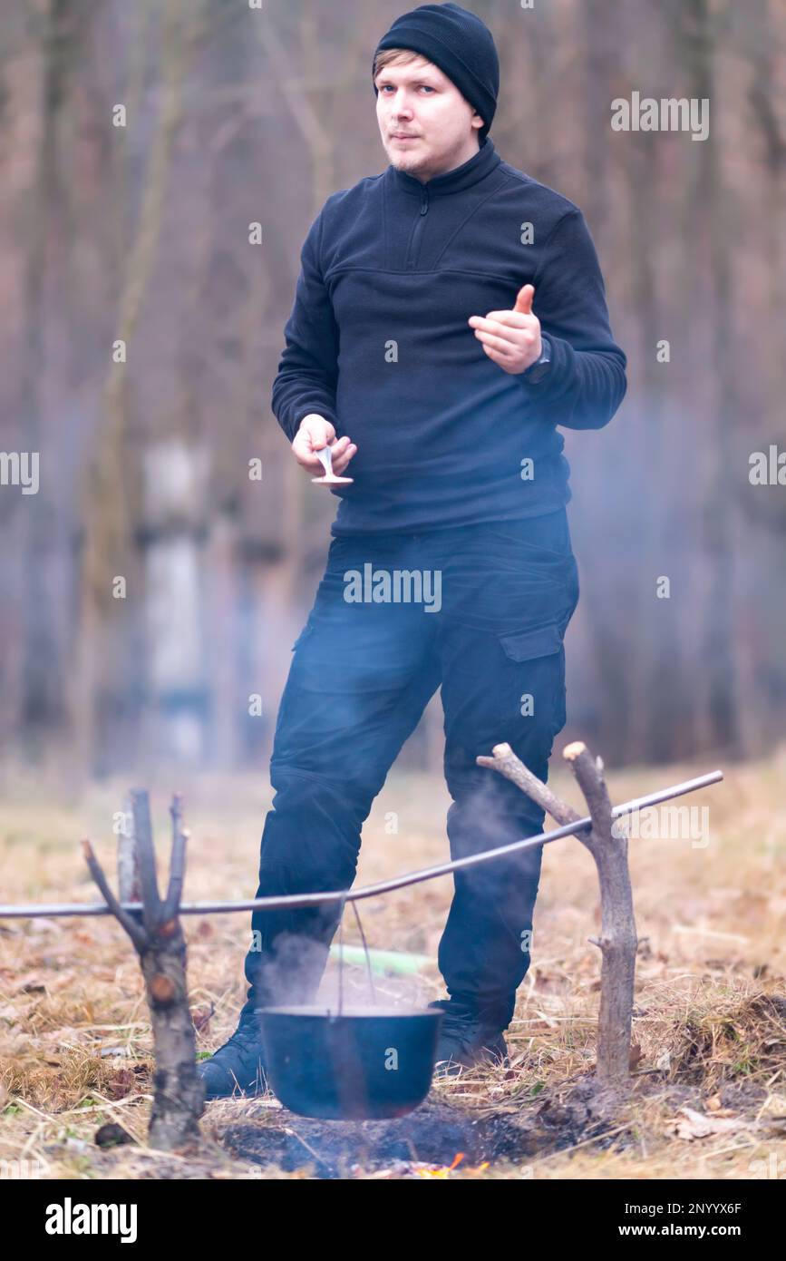 A young man in black, tactical clothes, stands thinking by the fire ...