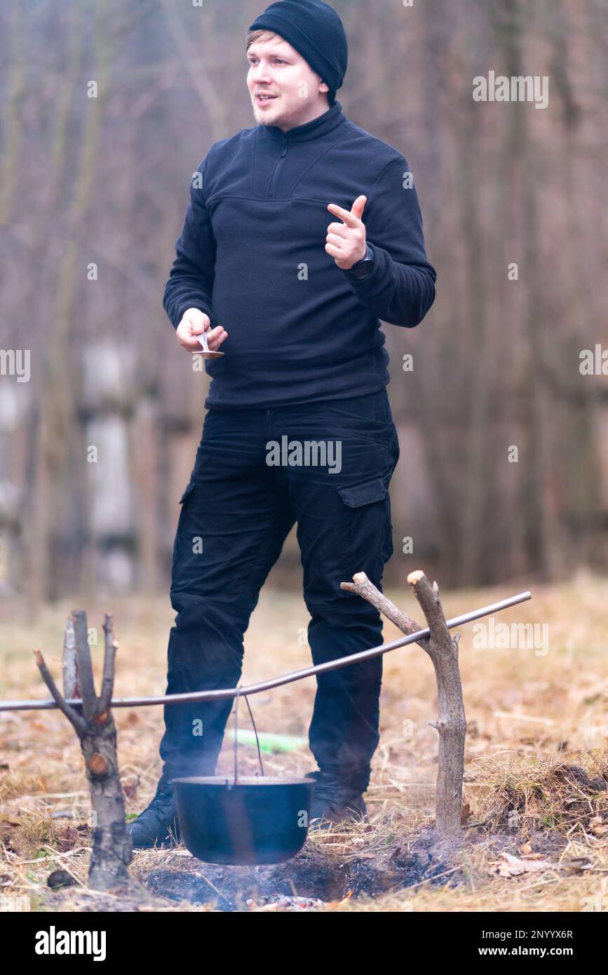 The guy, holding a large spoon in his hand, stands by the fire with ...