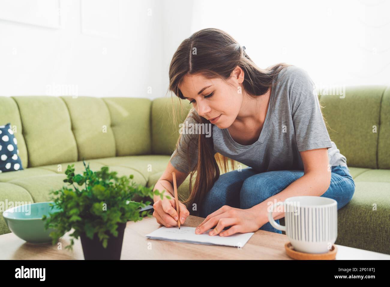 Woman leaning down on the coffee table writing an address on the letter ...