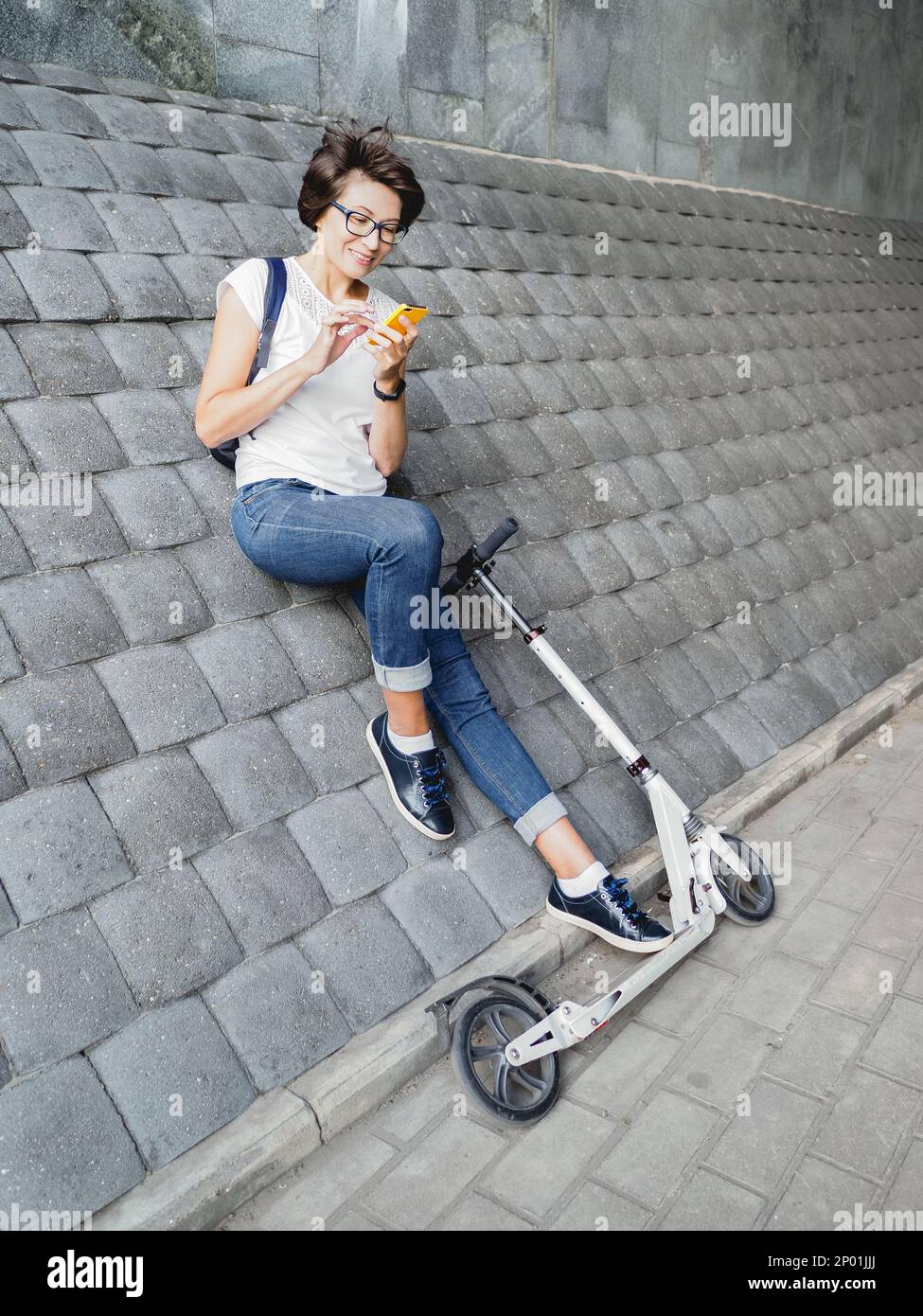 Smiling Woman Texting On Smartphone After Riding Kick Scooter Female In Jeans And Sneakers On