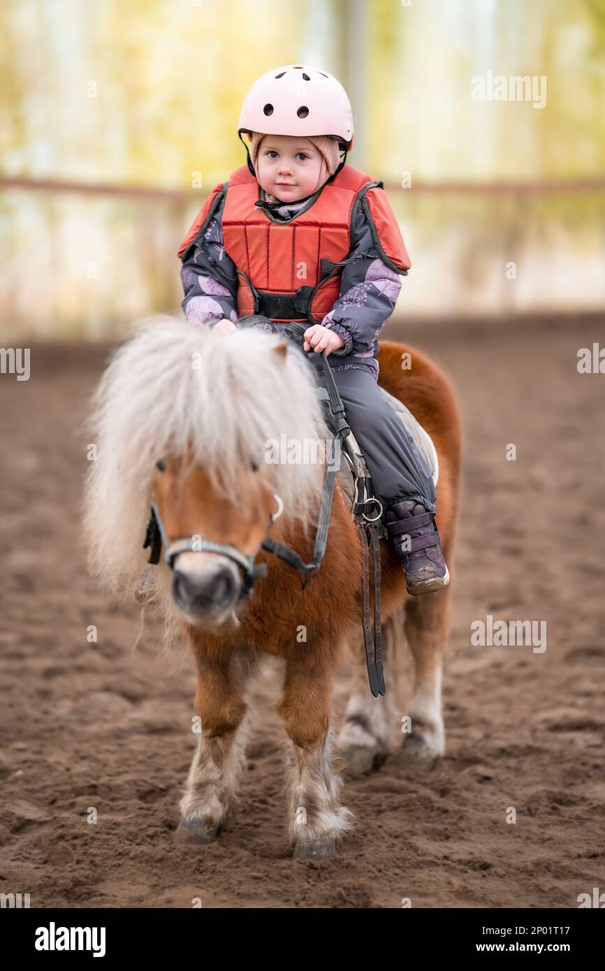 Little Child Riding Lesson. Three-year-old girl rides a pony and does ...