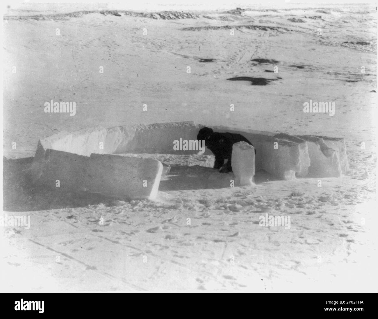 Eskimo building an igloo; completing the first layer of ice blocks ...