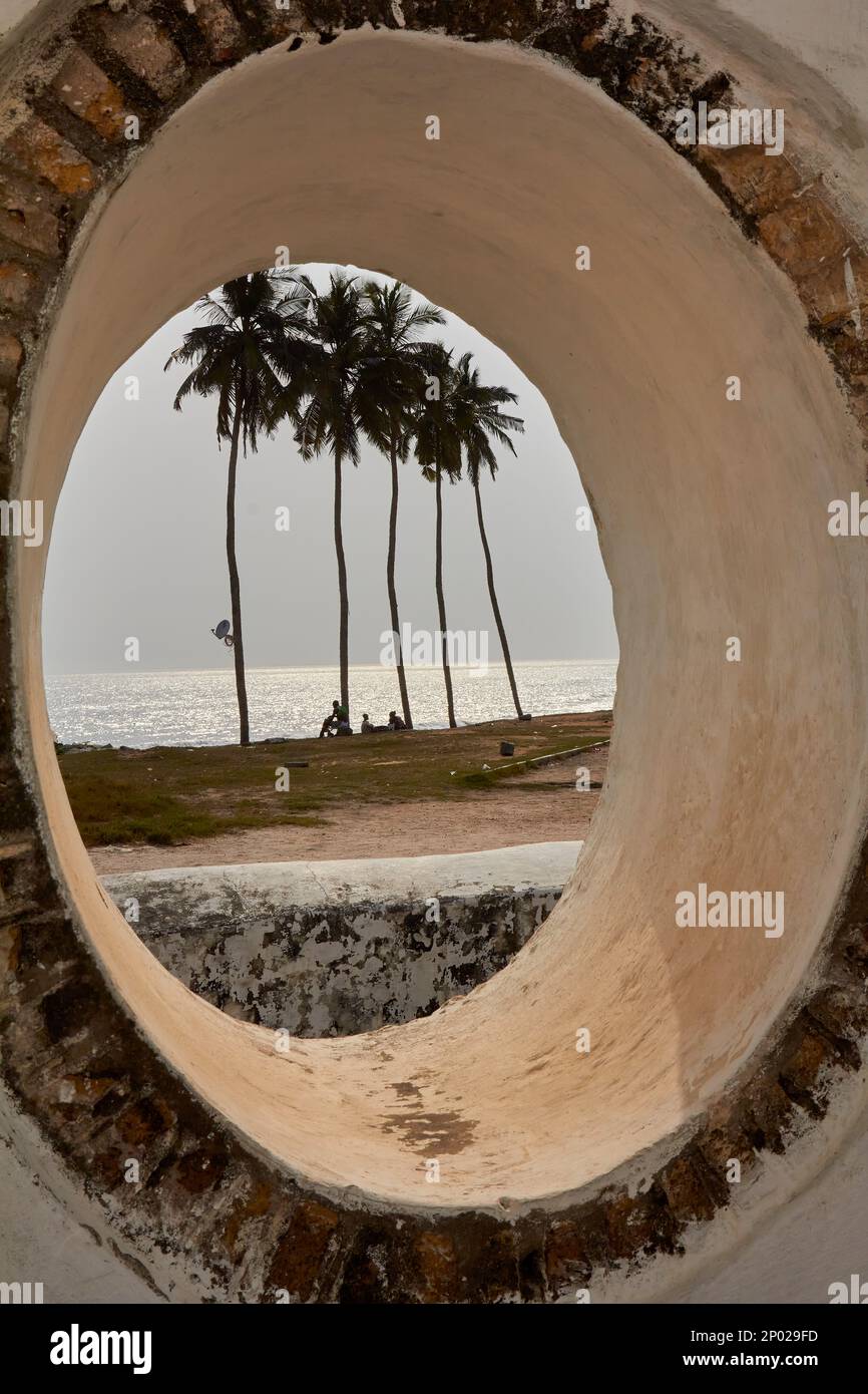 View of palm trees and sea through a stone window at Elmina Castle ...