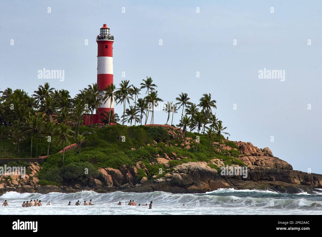 Tourists swimming at Lighthouse Beach with the Vizhinjam Lighthouse in the background in Kovalam ...