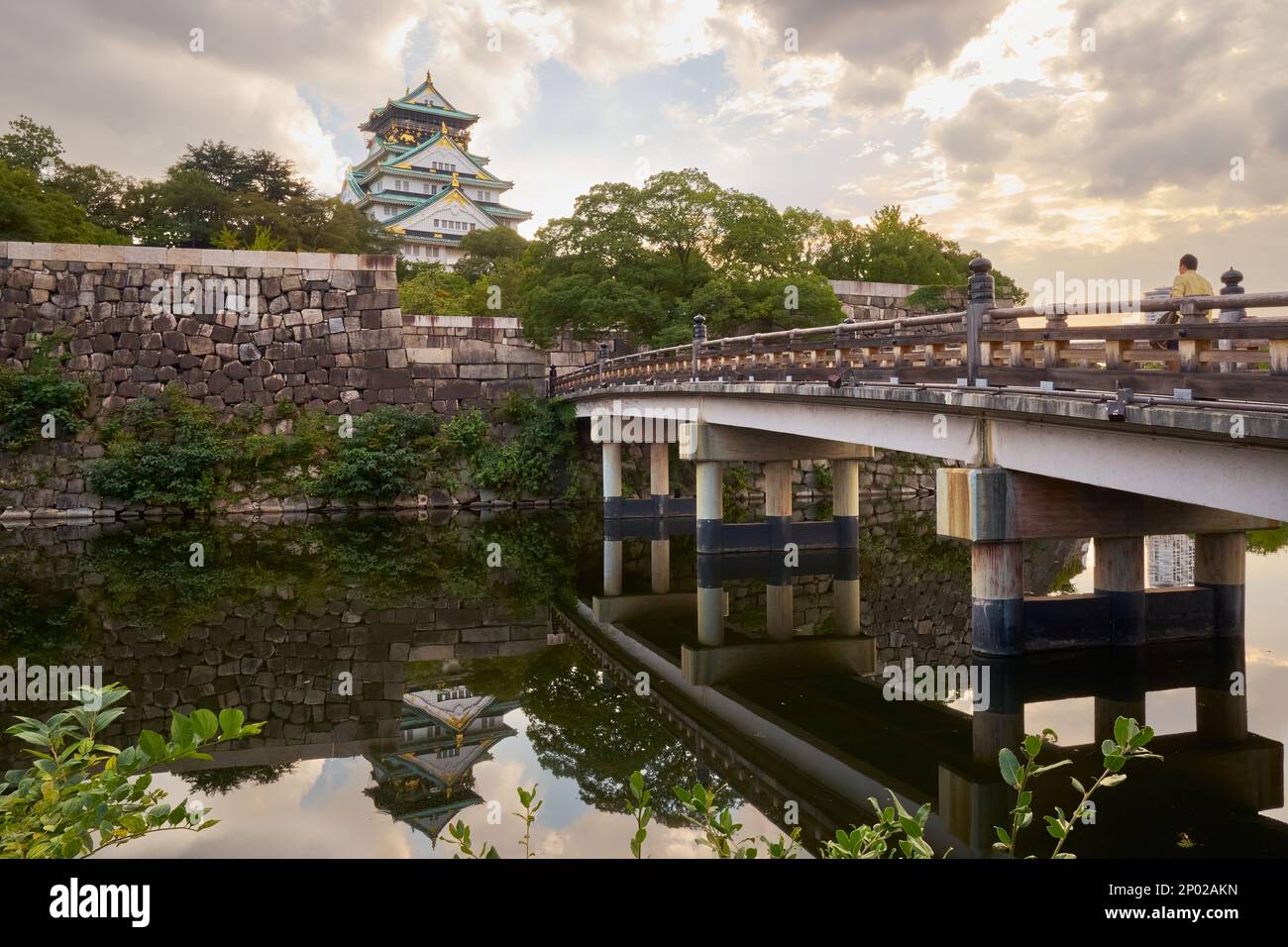 A moat bridge with castle reflections in the water leading up to the ...
