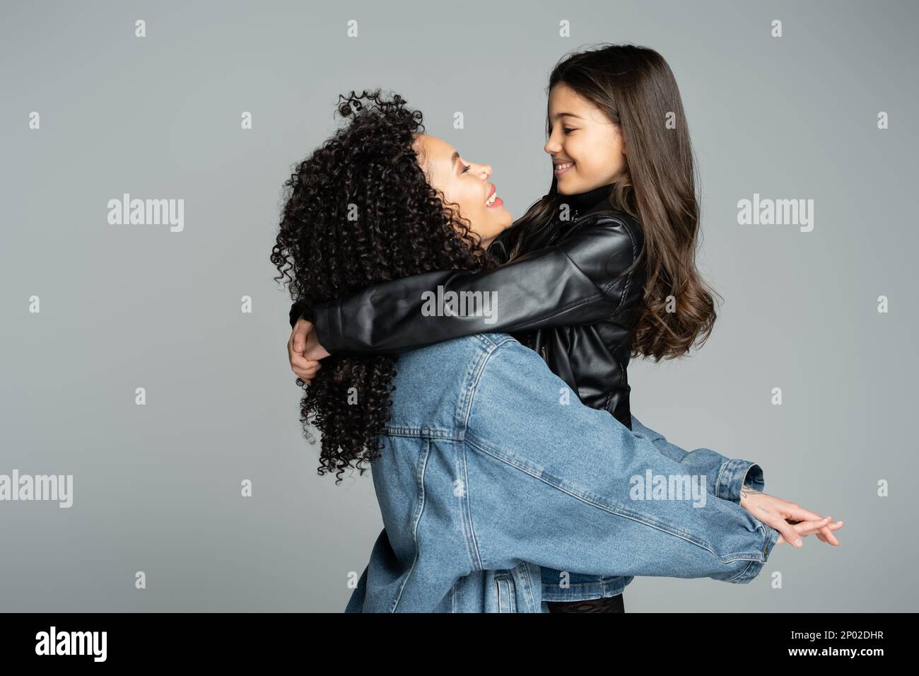 Side view of smiling mom in denim jacket hugging cheerful child ...
