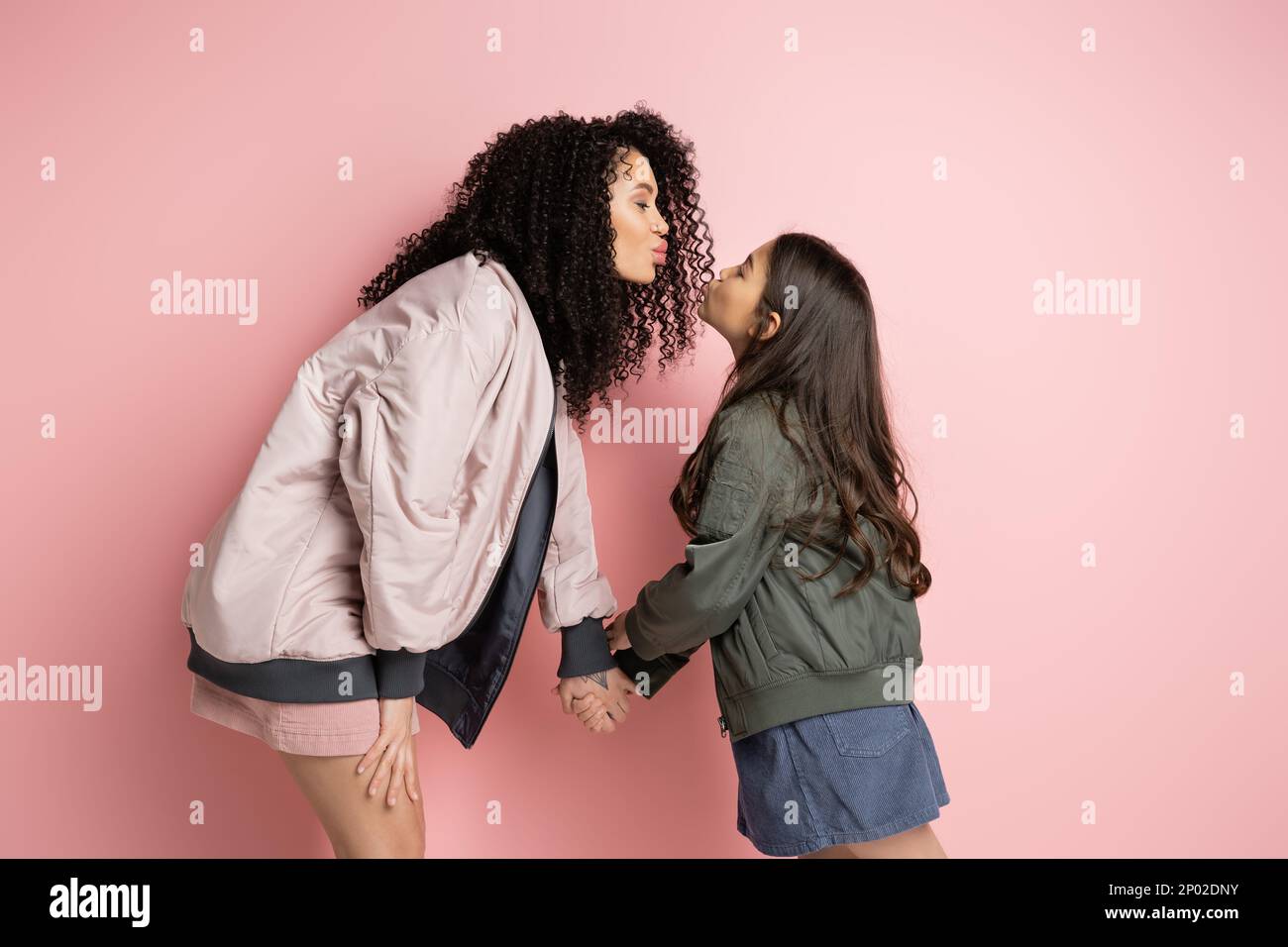 Side view of stylish woman and child pouting lips on pink background ...