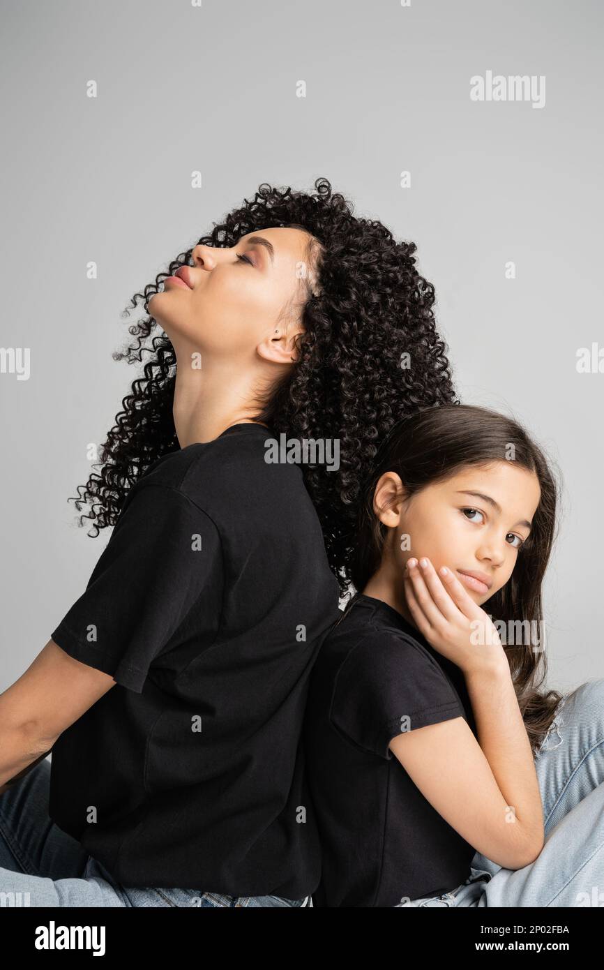 Curly mother and daughter in black t-shirts sitting back to back ...