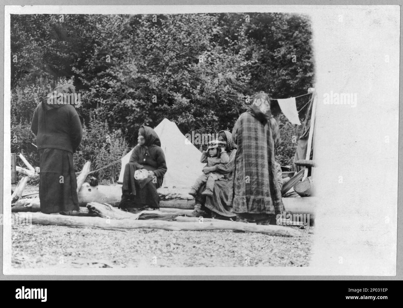 Four women and an infant, sitting on and standing near logs. Frank and ...