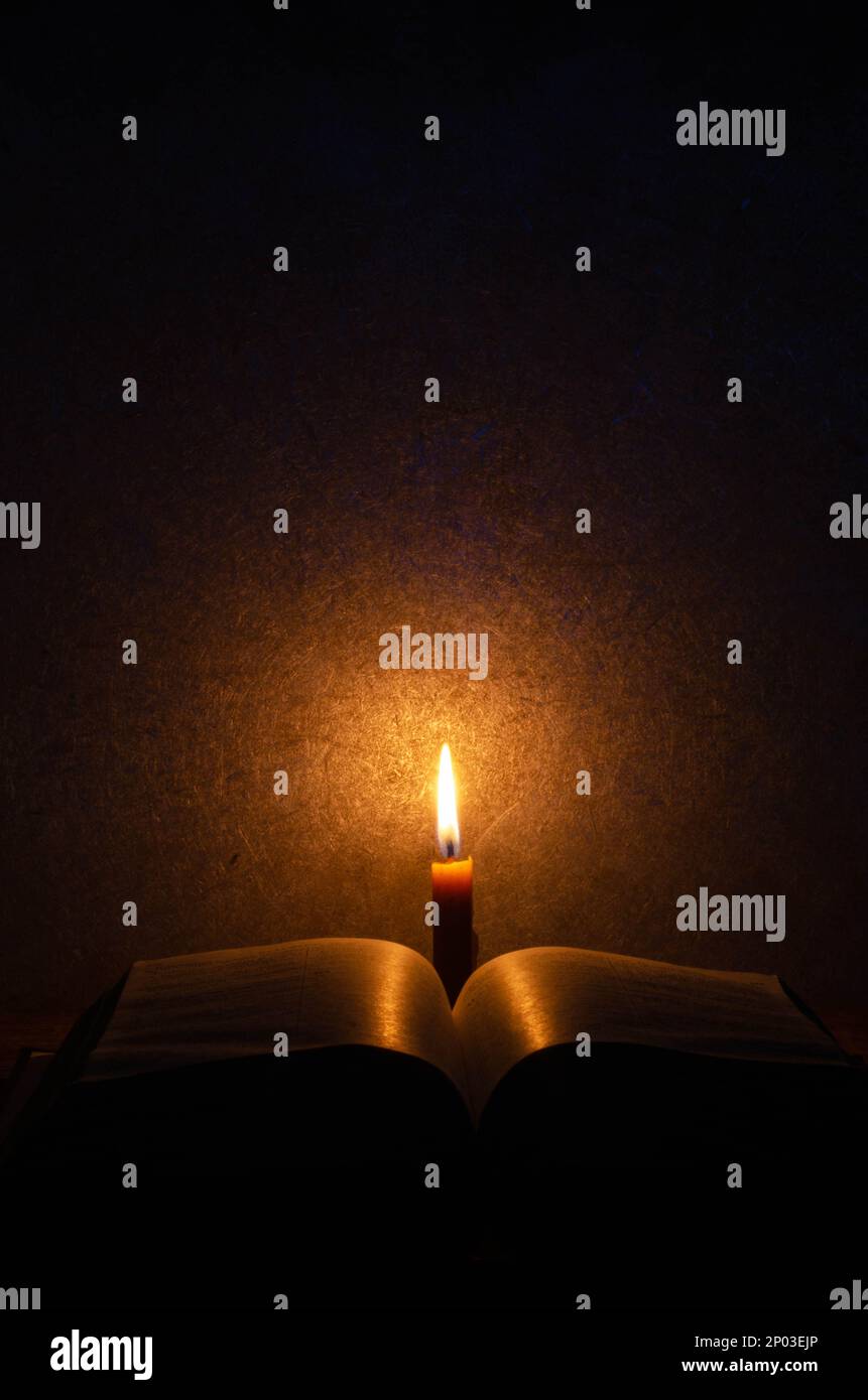 Burning candle on an open book in dark room with copy space. reading a ...