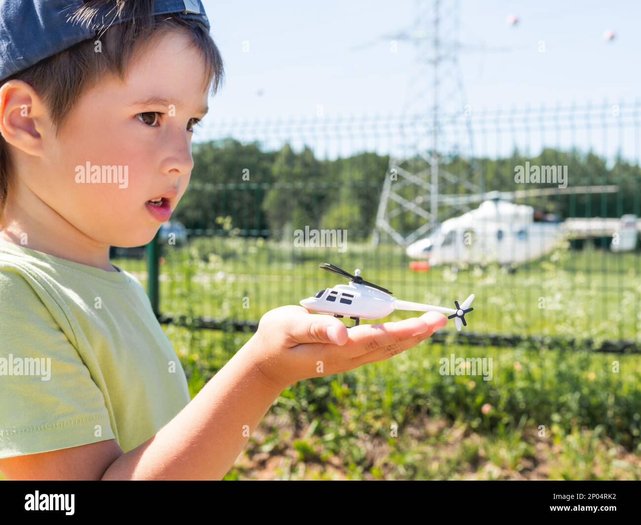 Little boy holds toy helicopter in front of real one on helipad. Kid ...