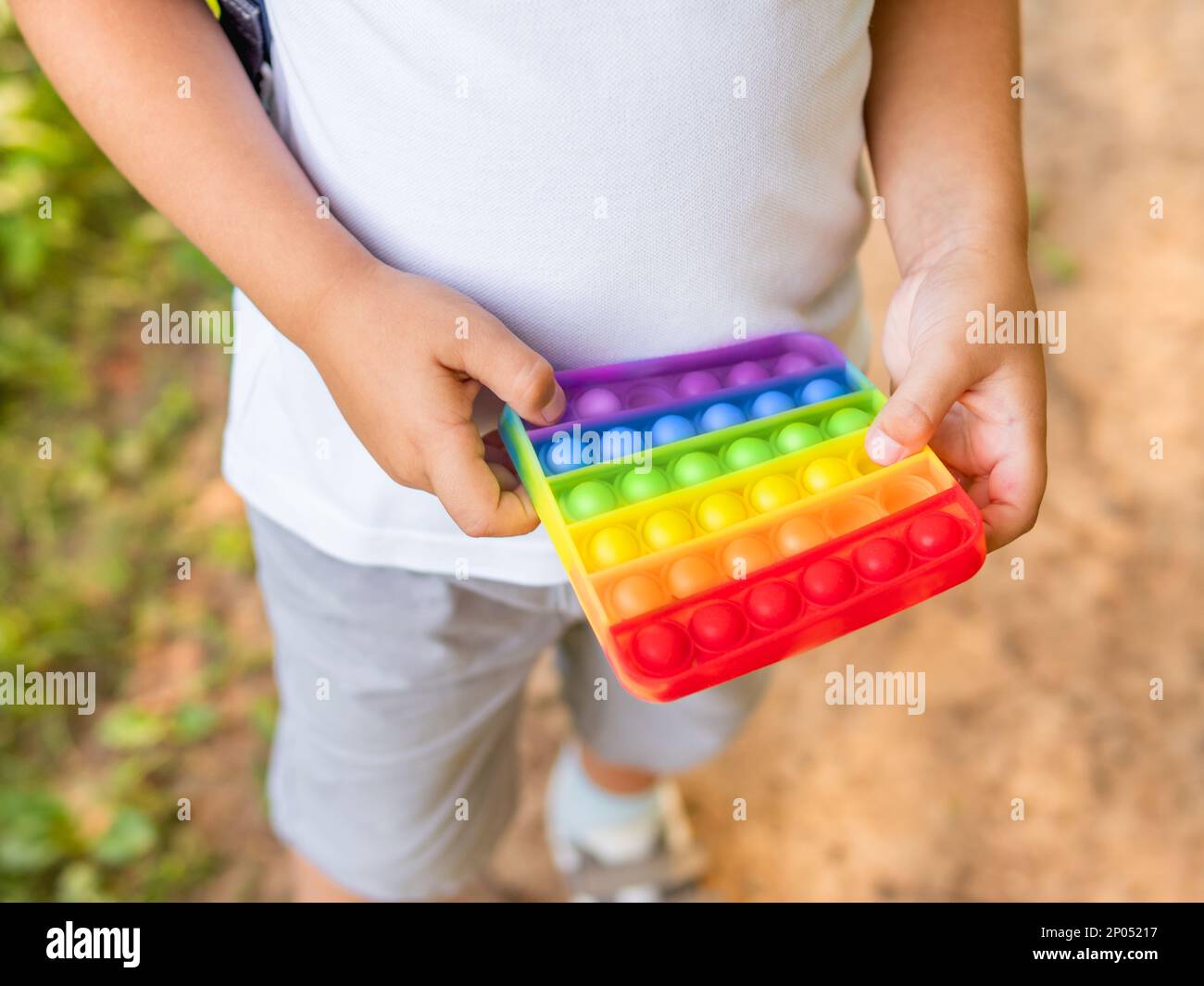 Little boy plays square rubber fidget toy Pop It. Rainbow-colored anti ...