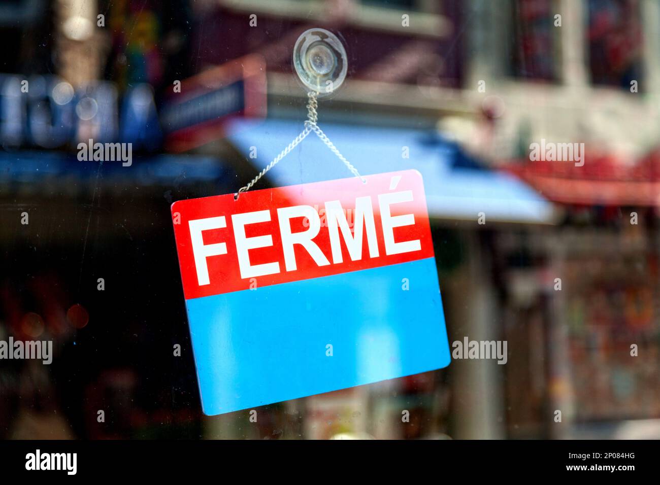 Red and blue sign in the window of a shop saying in French "Fermé ...