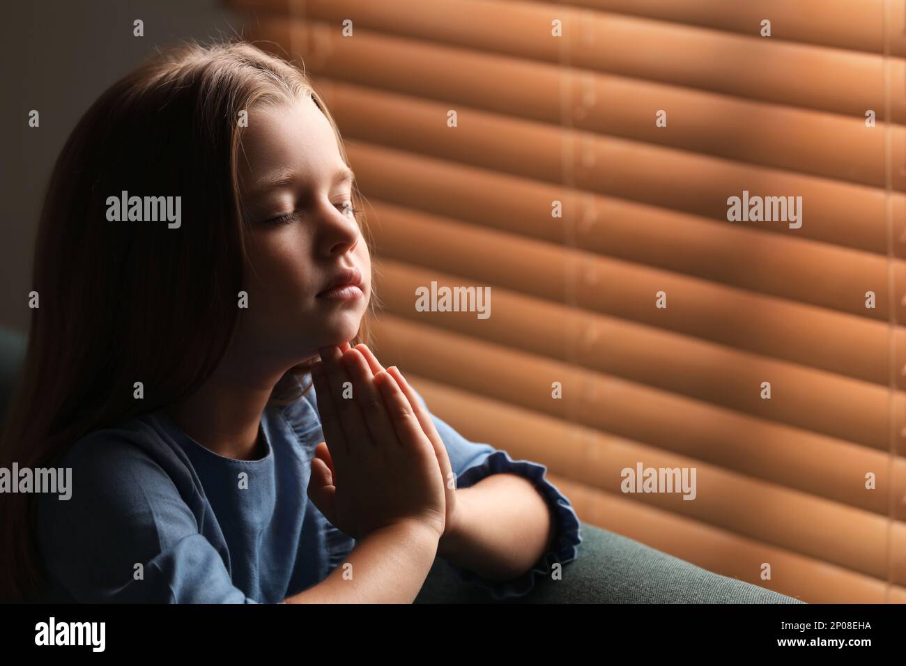 Cute little girl praying near window. Space for text Stock Photo - Alamy
