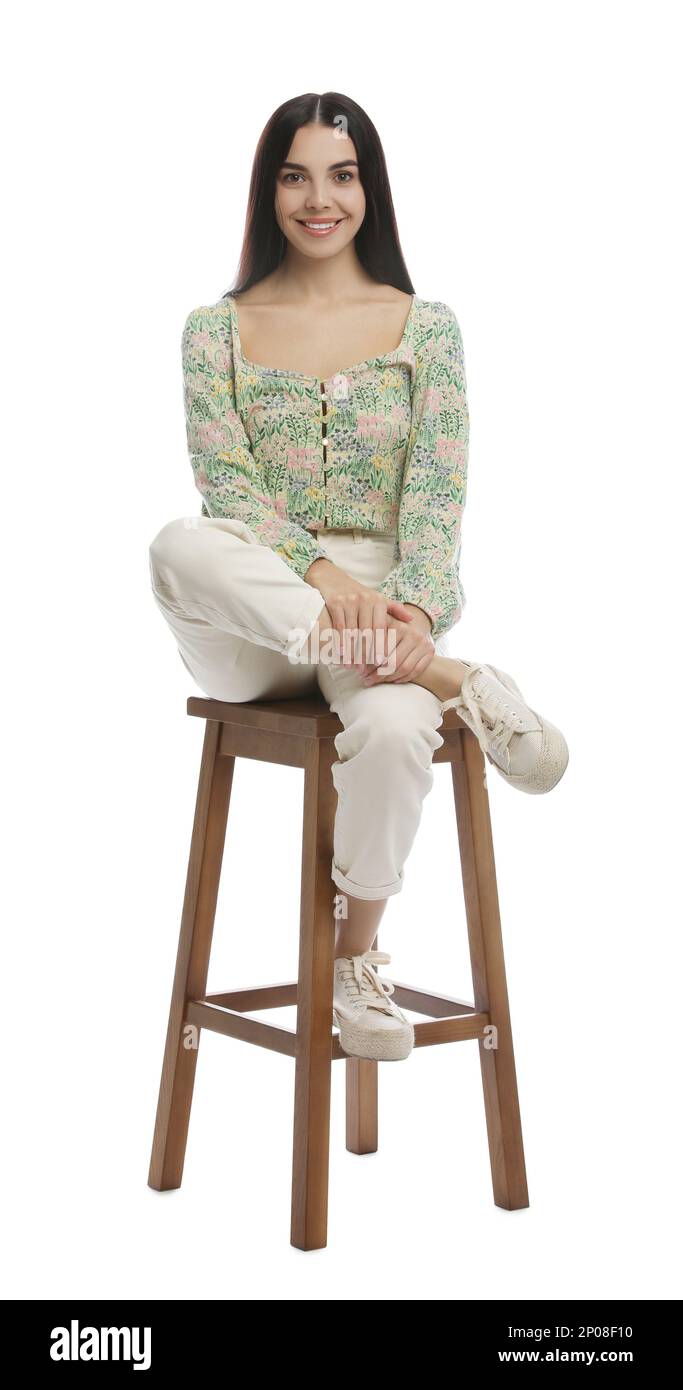 Beautiful young woman sitting on stool against white background Stock ...