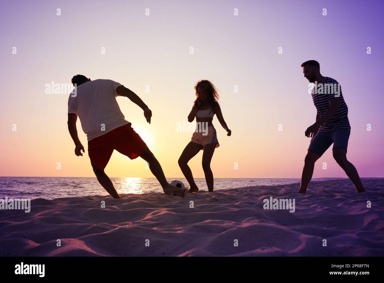 Friends playing football on beach at sunset Stock Photo - Alamy