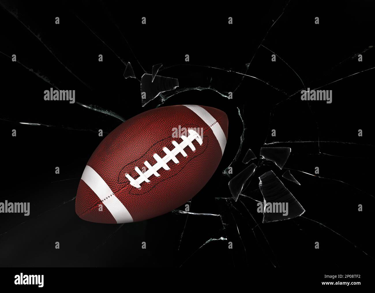 American football ball breaking up glass against black background Stock ...
