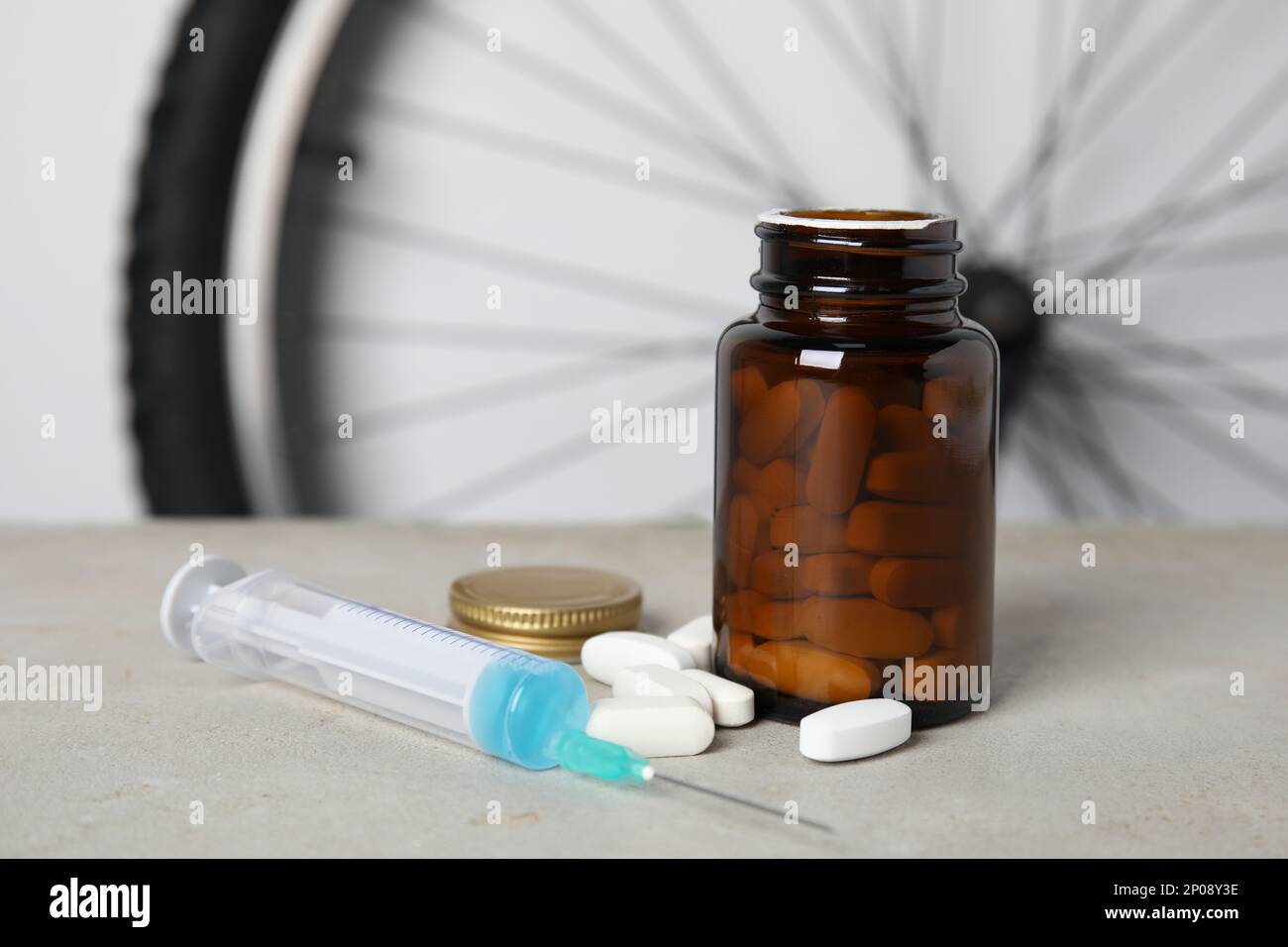 Pills and syringe on light grey table near bike wheel. Using doping in ...