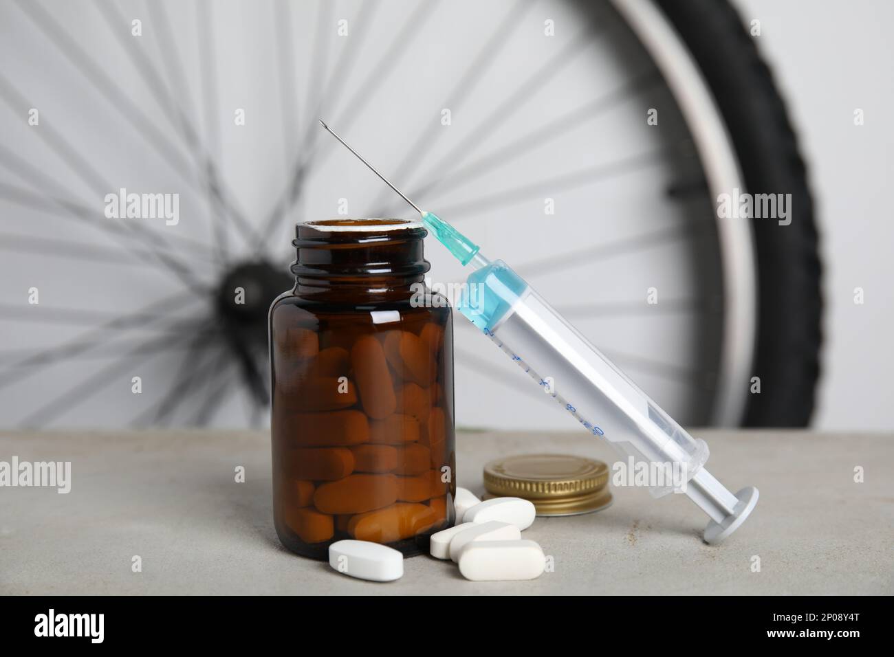 Pills and syringe on light grey table near bike wheel. Using doping in ...