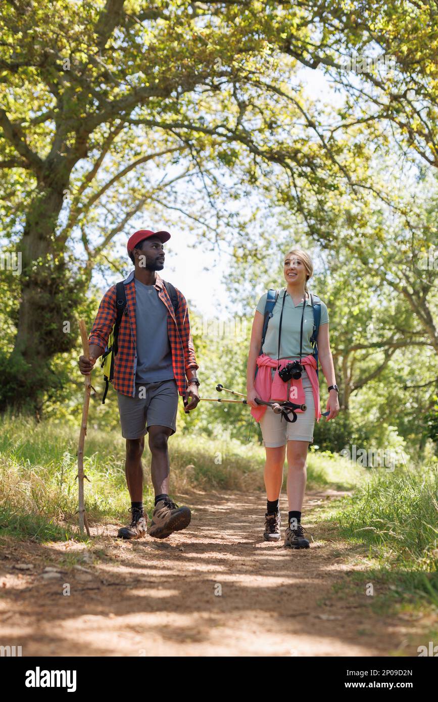Vertical of happy, diverse couple walking on path though sunny forest ...
