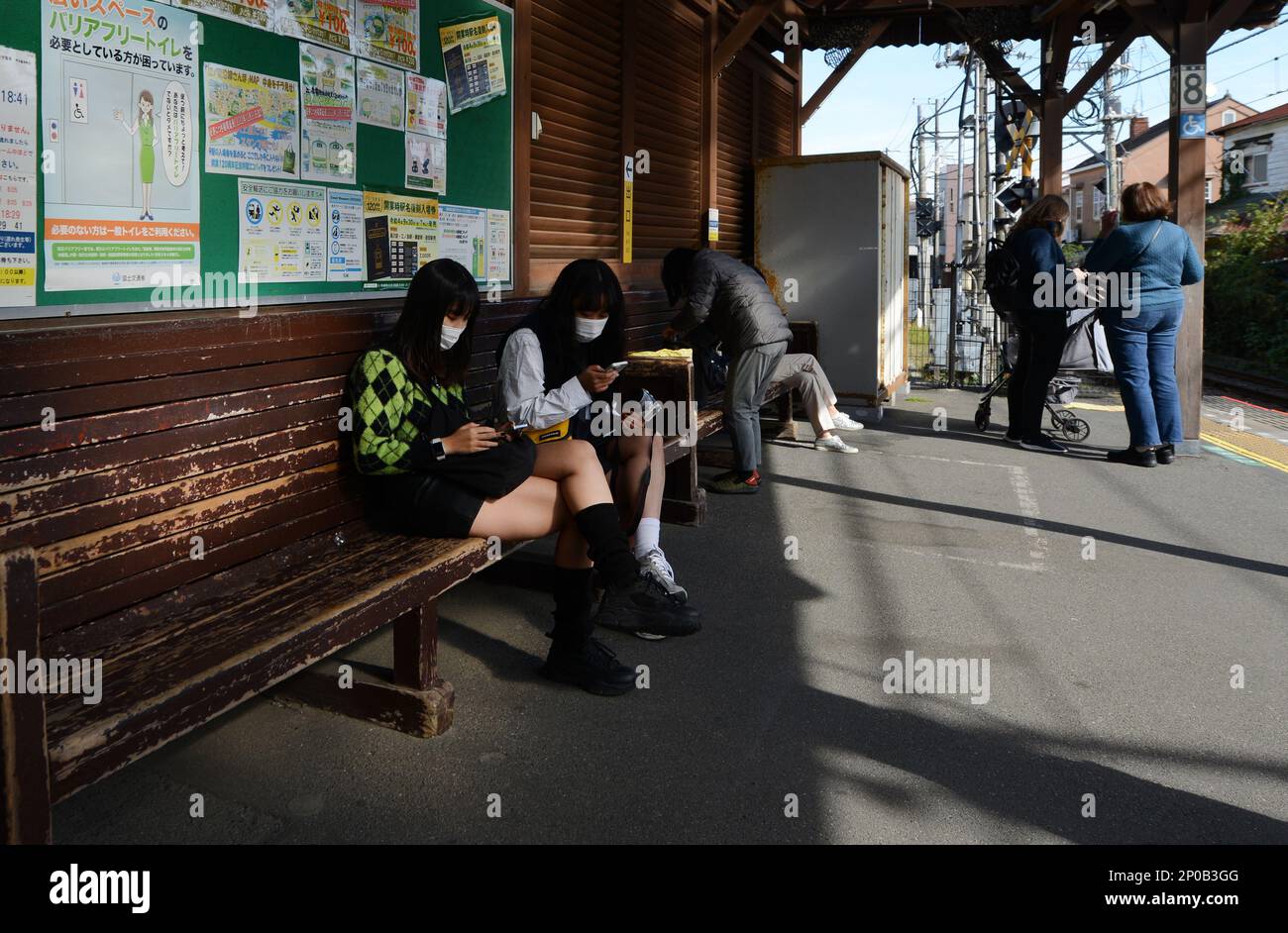 Young Japanese women sitting on an old wooden bench at the train ...