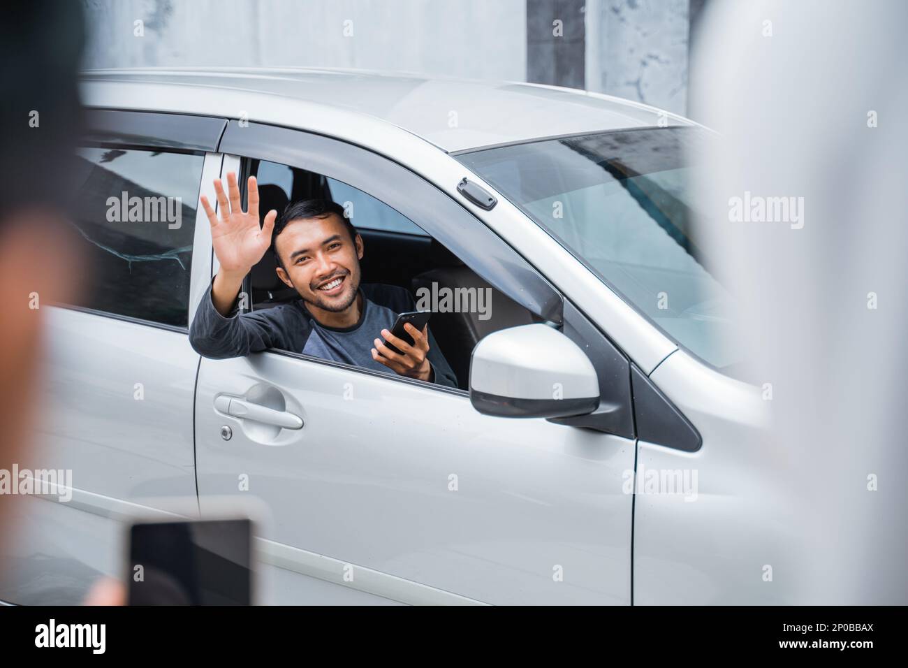 male driver in a car holding waving as meets customers Stock Photo - Alamy
