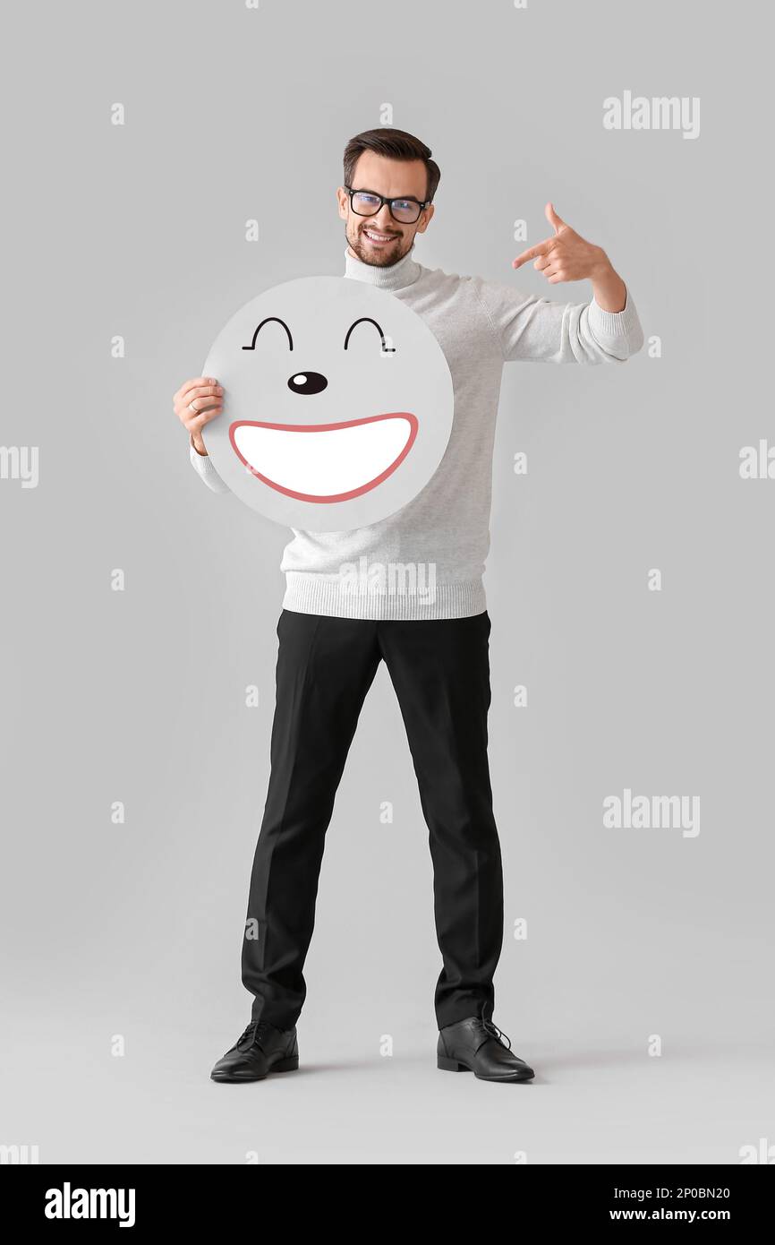 Happy man holding paper with smiling emoticon on light background Stock ...