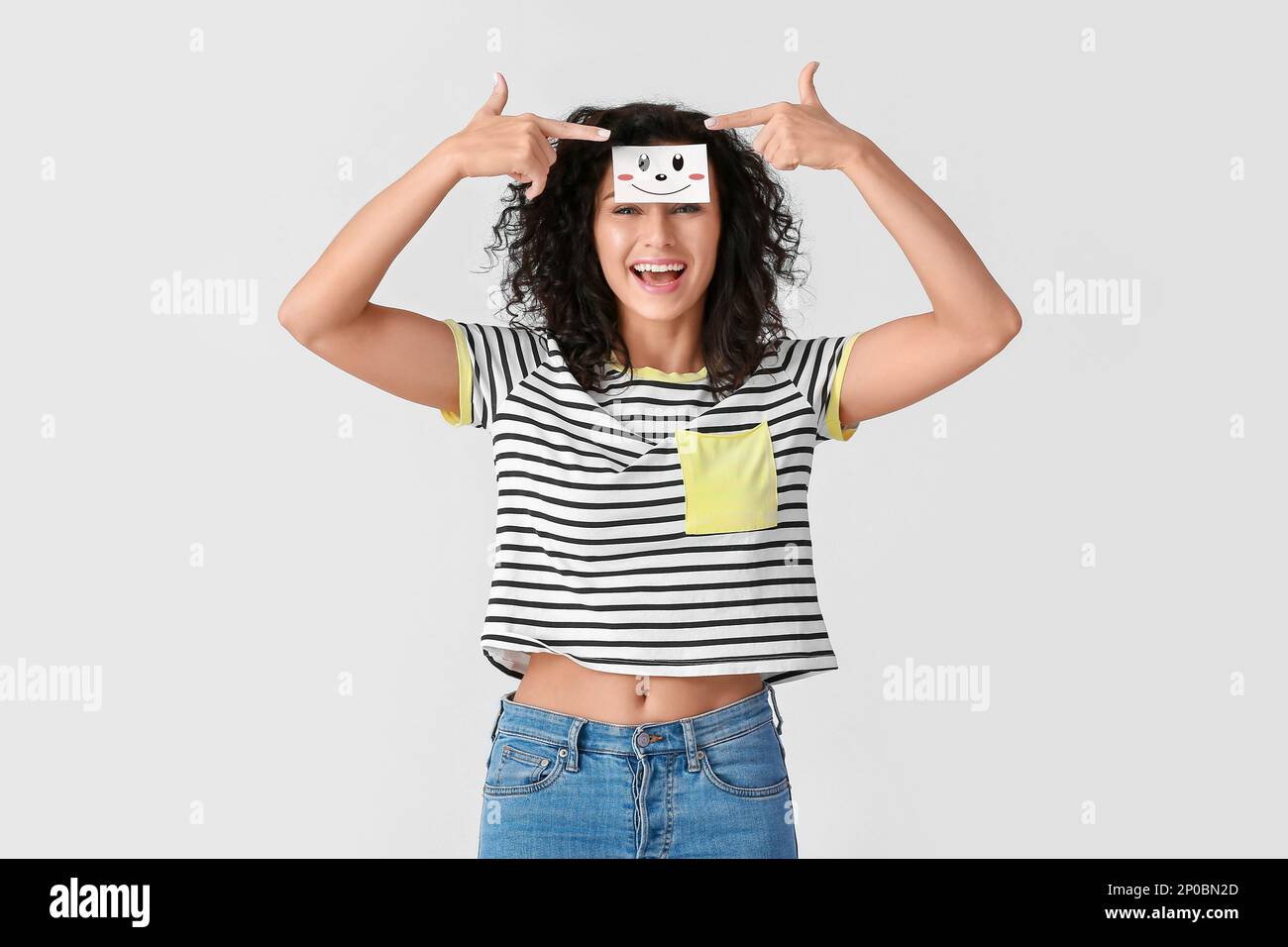 Happy young woman with smiling emoticon on her forehead against light ...