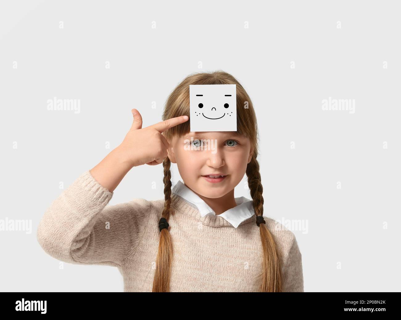 Little girl with happy emoticon on forehead against light background ...