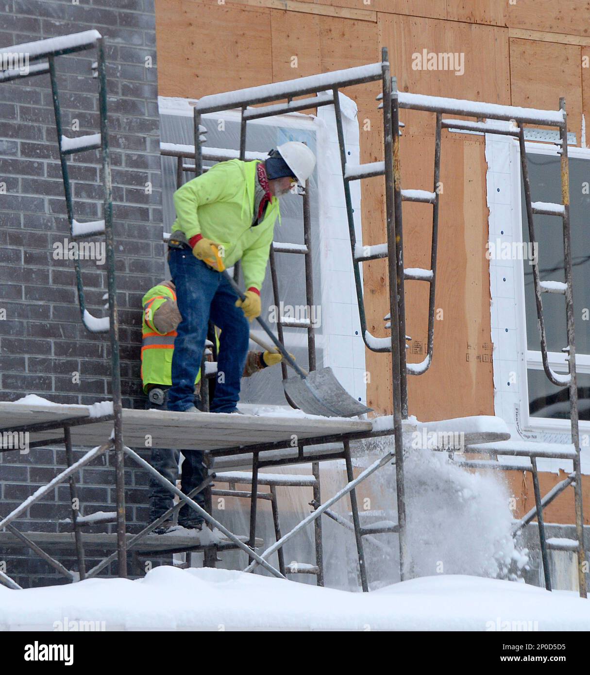 Construction worker shovels snow from latest storm off scaffolding on ...