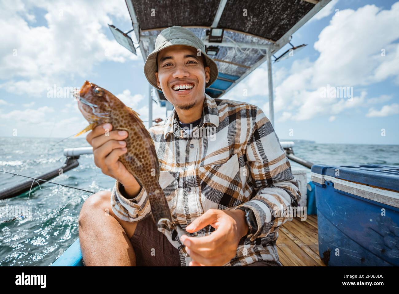 smiling Asian angler holding a grouper on small fishing boat Stock ...
