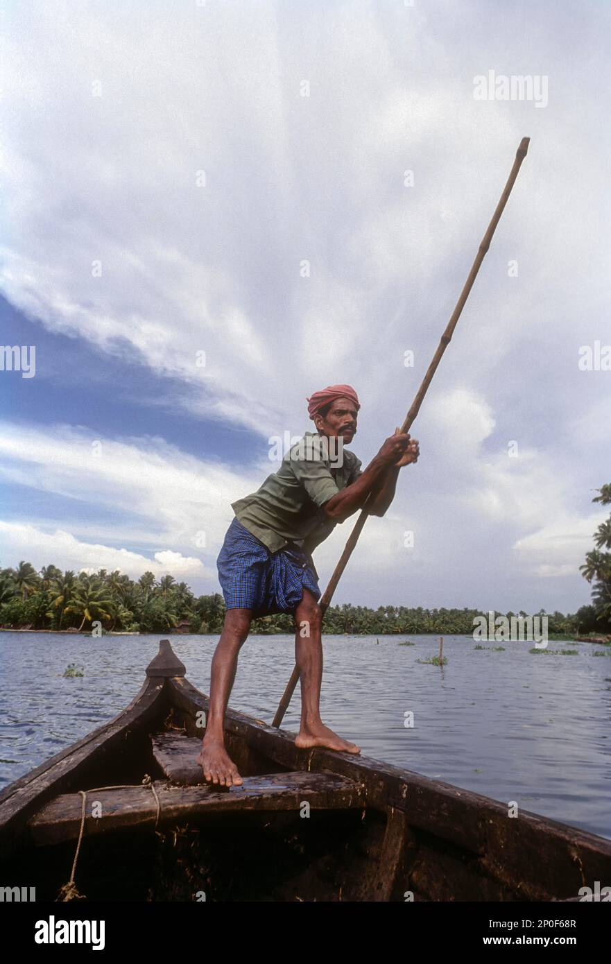Boatman with a punt pole on a boat in the backwaters of Kerala, India ...